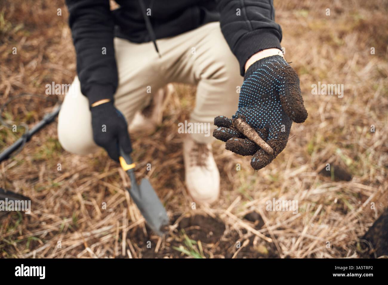 Sitting, holding old bullet. Man is with metal detector in the field ...