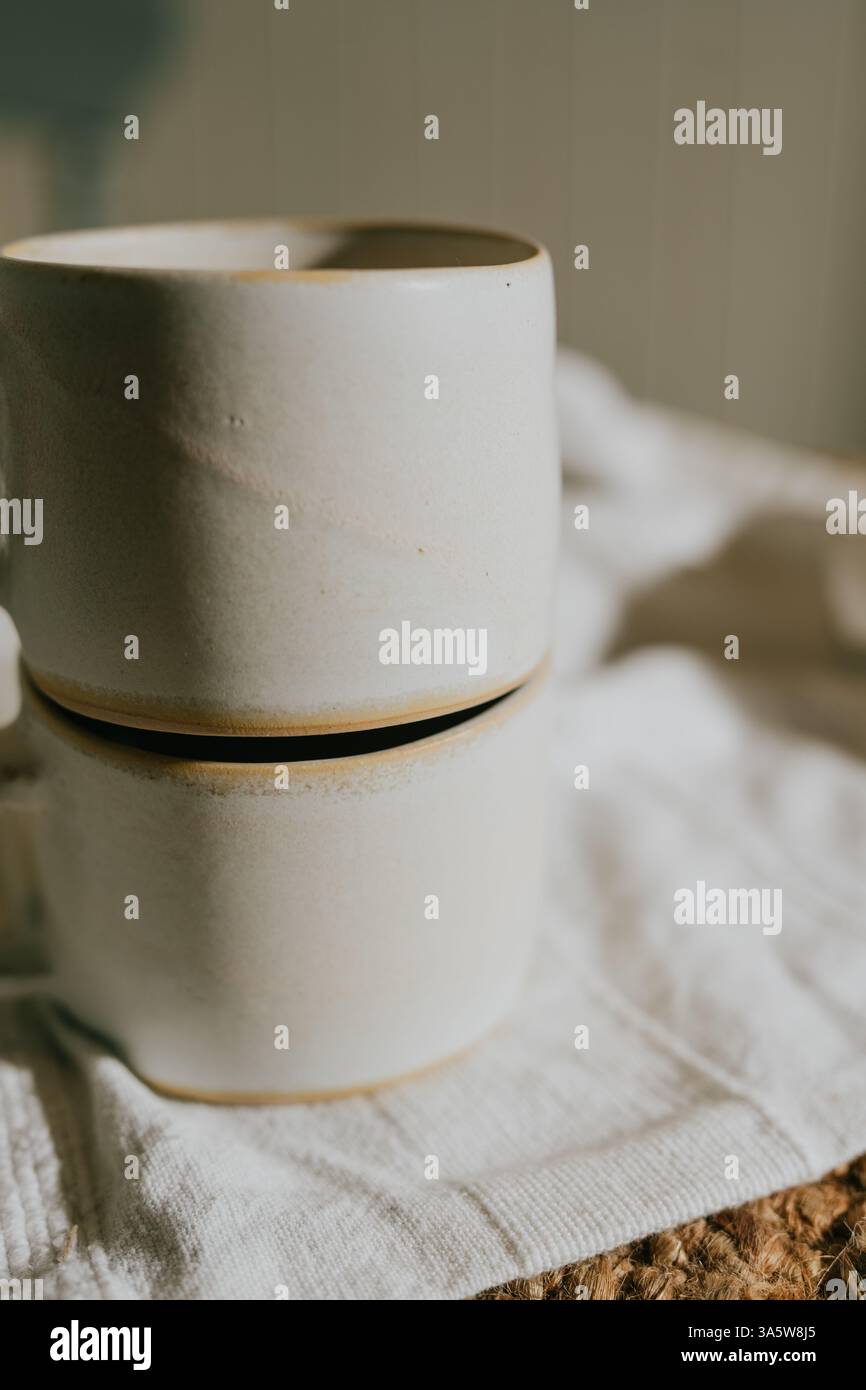Two white ceramic cups sit on a white cloth. The cups are identical in ...