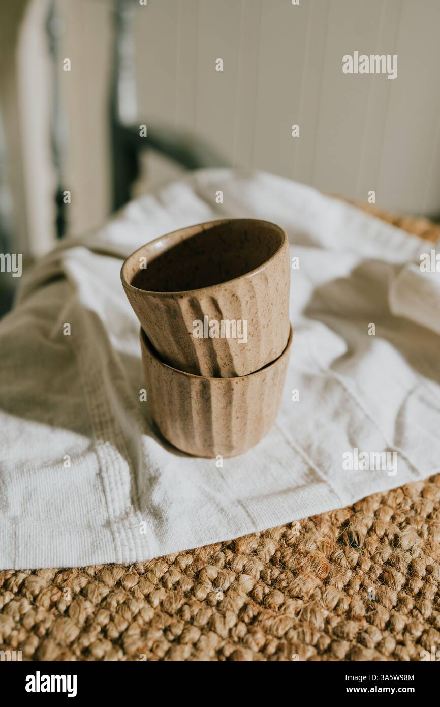 Two cups are sitting on a white cloth. The cups are brown and have a ...