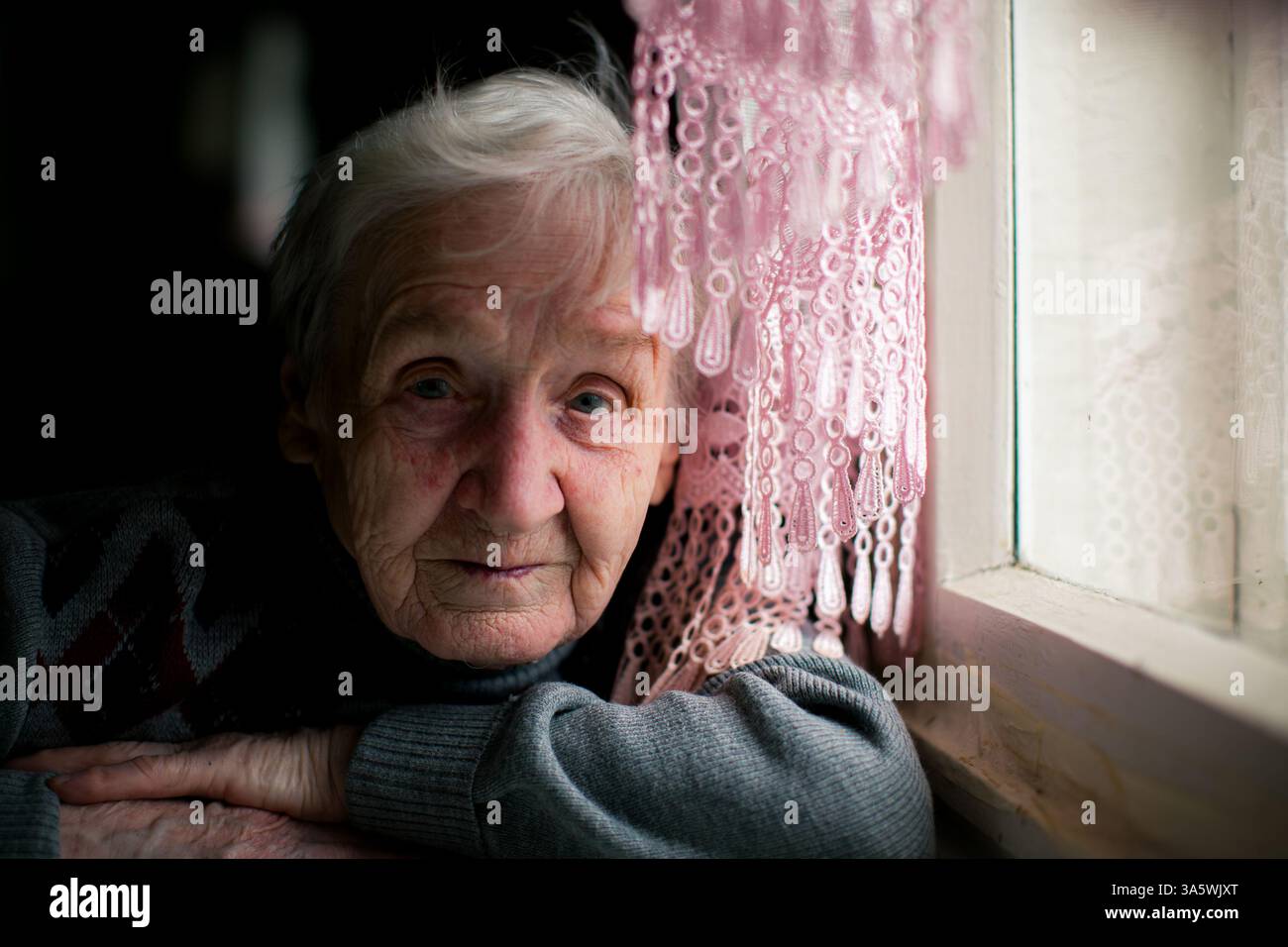 A portrait of an elderly woman sitting by the window in a rustic ...