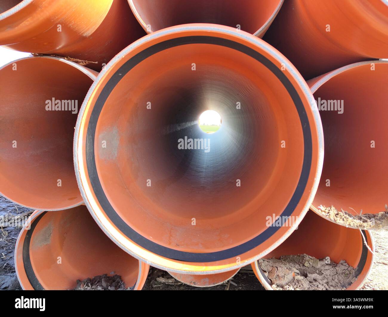 Stack of large orange industrial pipes with sunlight at tunnel end ...