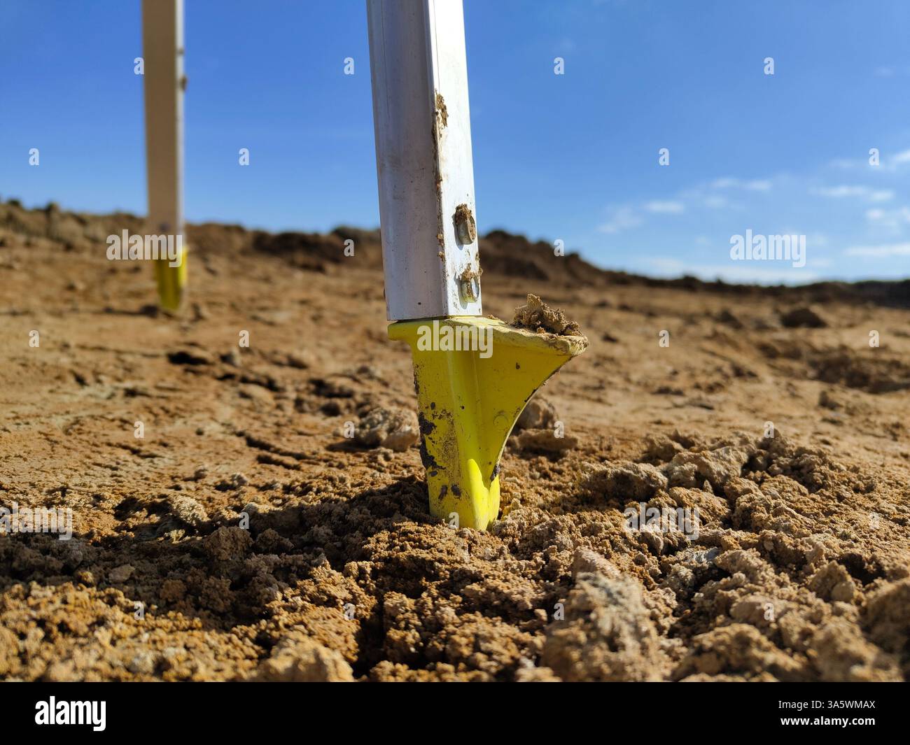 Close-up of construction stakes in sandy soil under clear blue sky ...