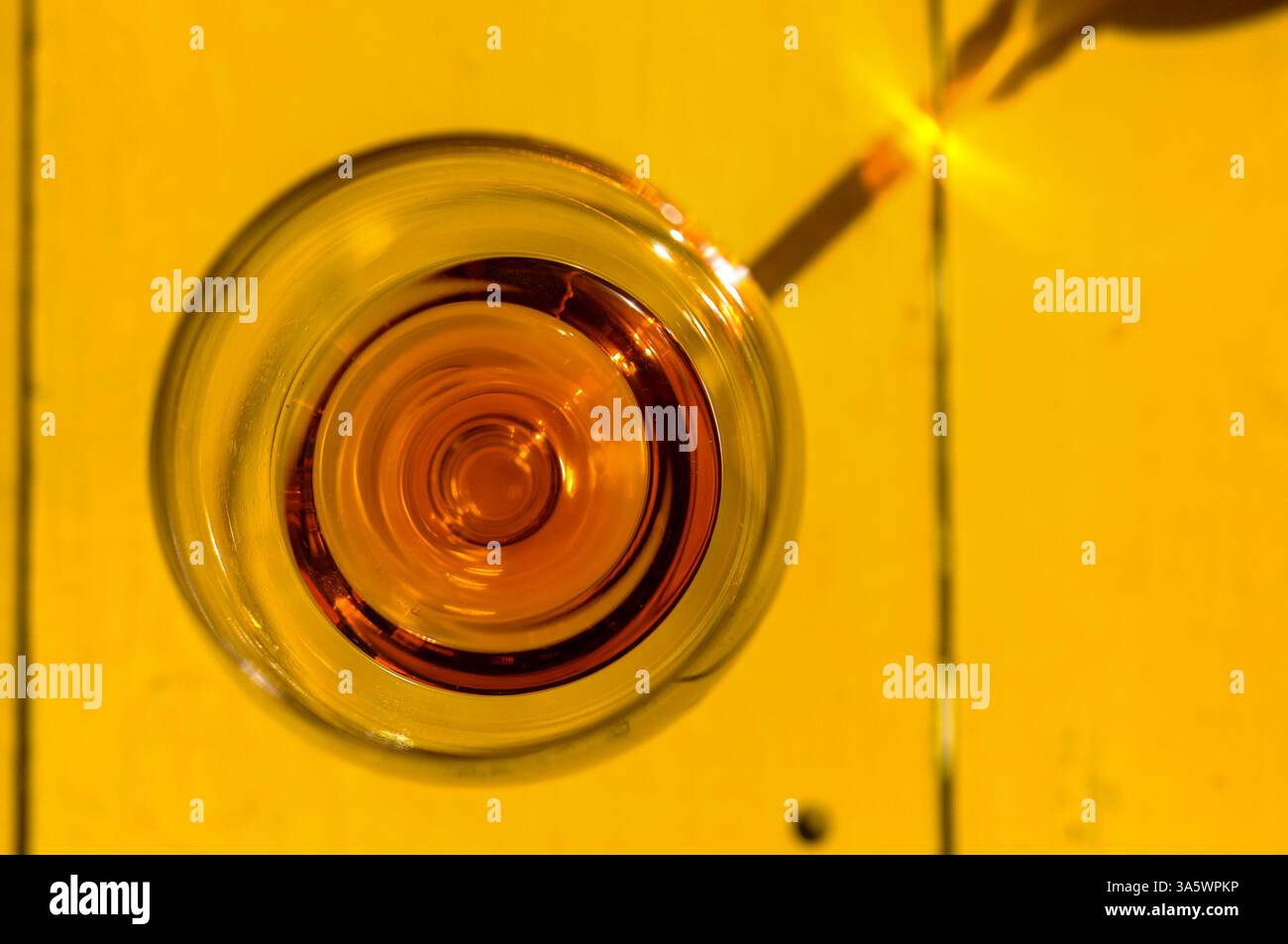 Aerial view of amber liquid in glass casting shadow on yellow surface ...