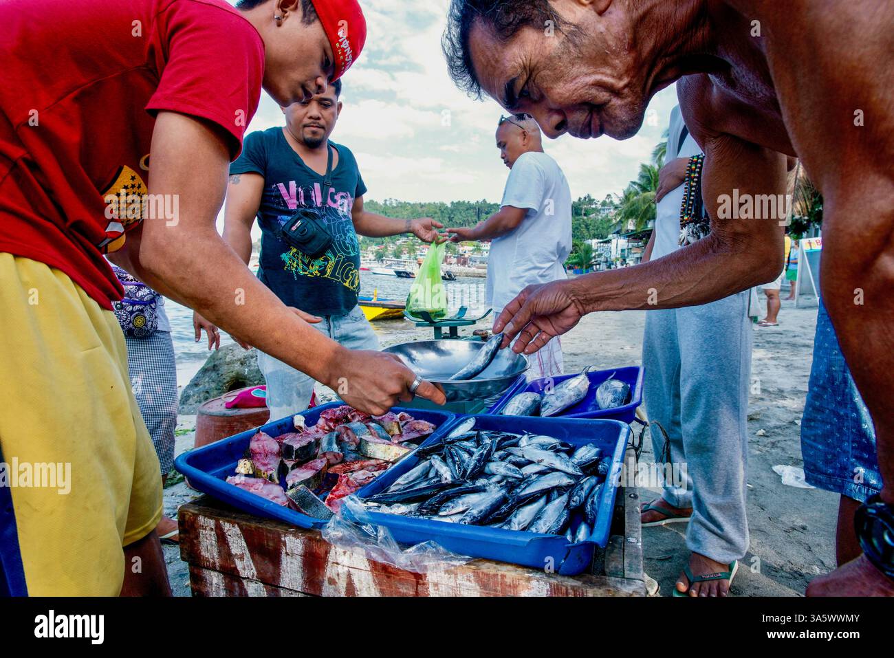 Locals buy fish from a seller on the beach at Puerto Galera, on Mindoro ...