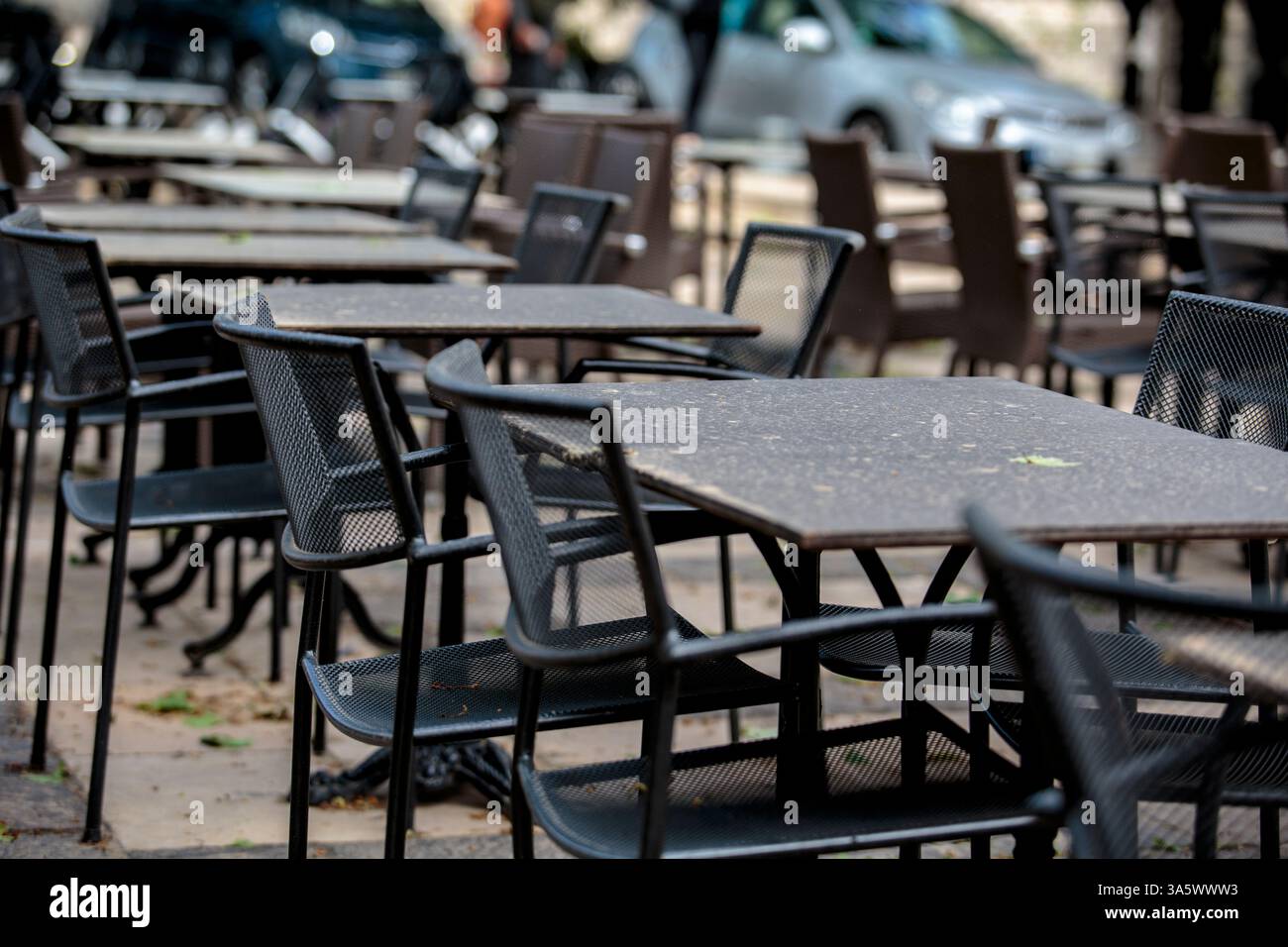 A quiet outdoor café with empty metal chairs and tables under the ...