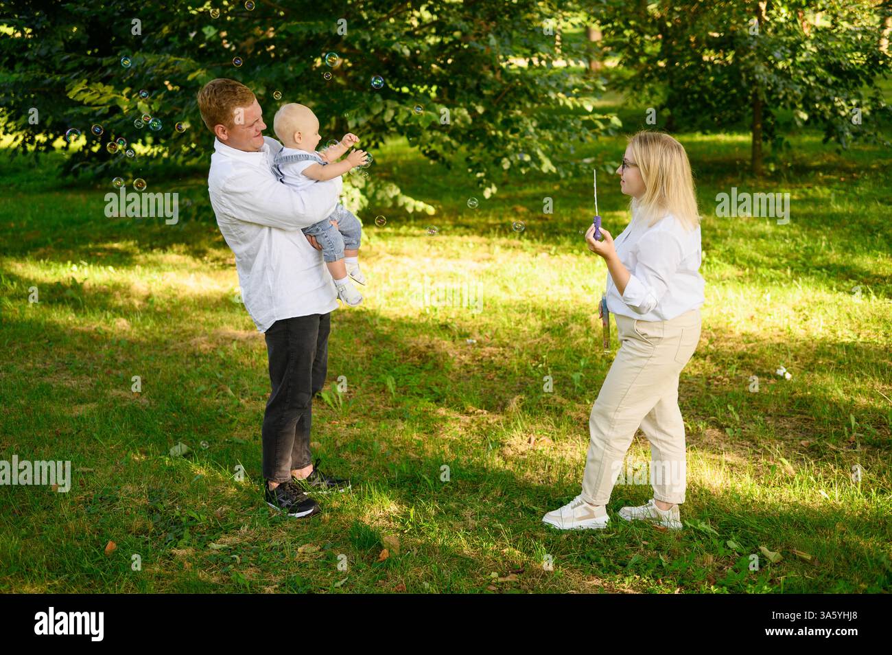 Parents and child spend summer weekends together in park. Mom blows ...