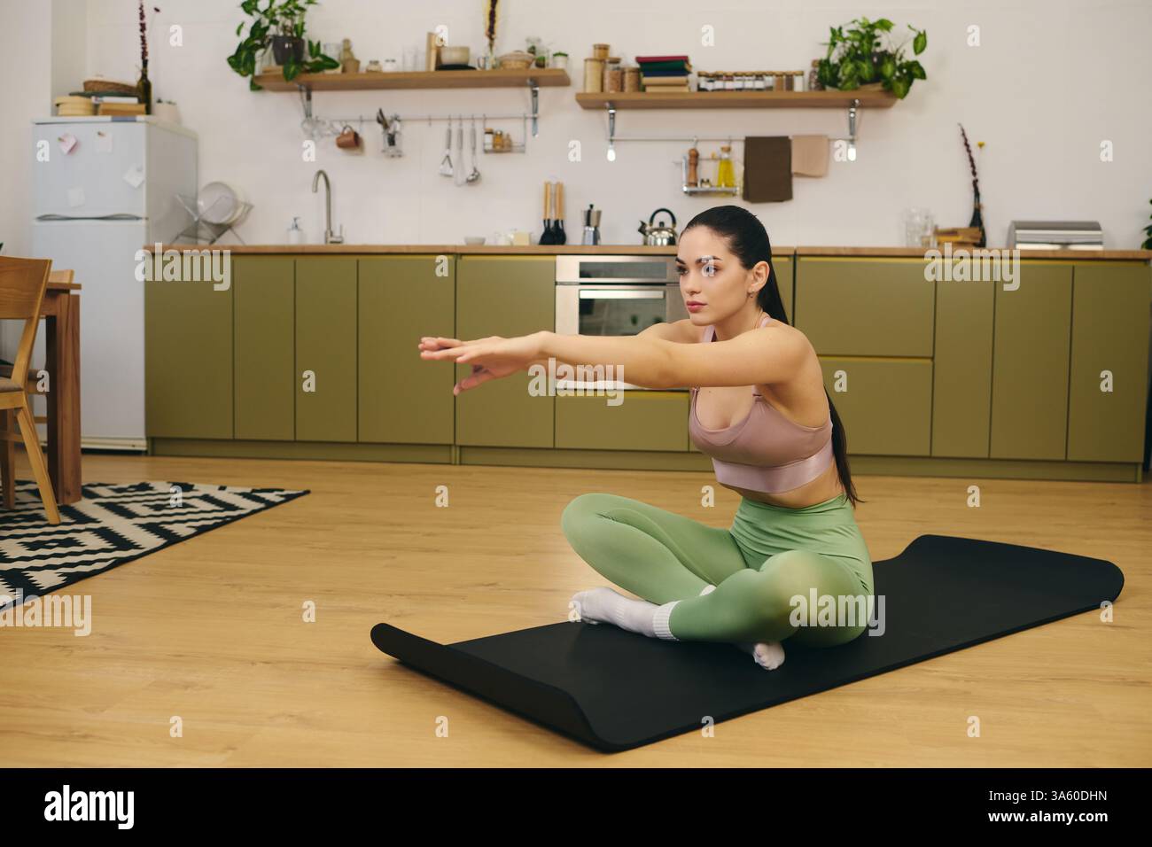 A beautiful young woman engages in a focused yoga pose on a mat in her ...