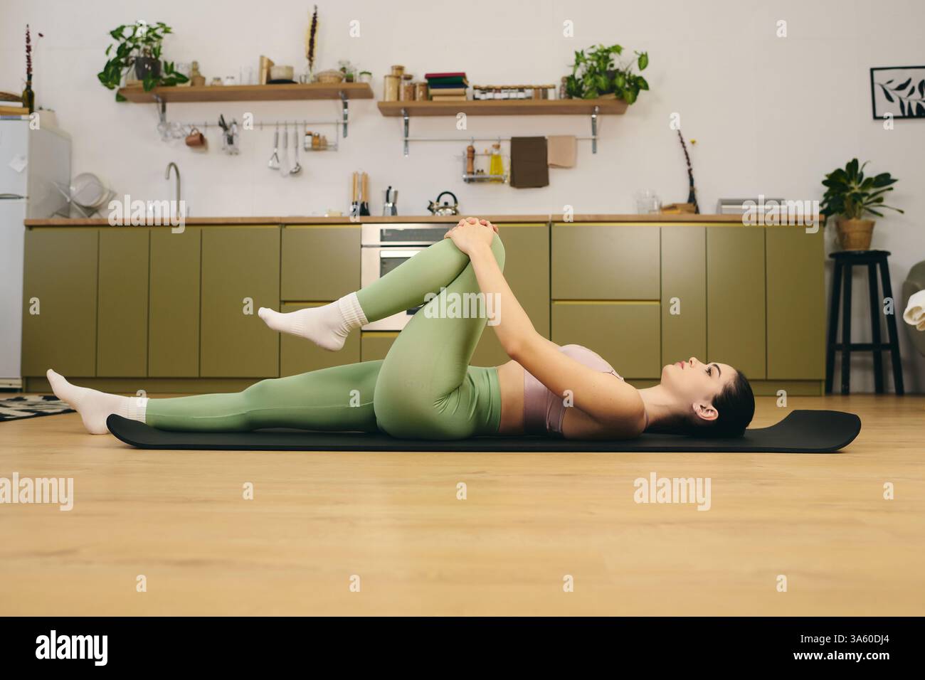 In a calm kitchen space, a young woman engages in yoga, fostering ...