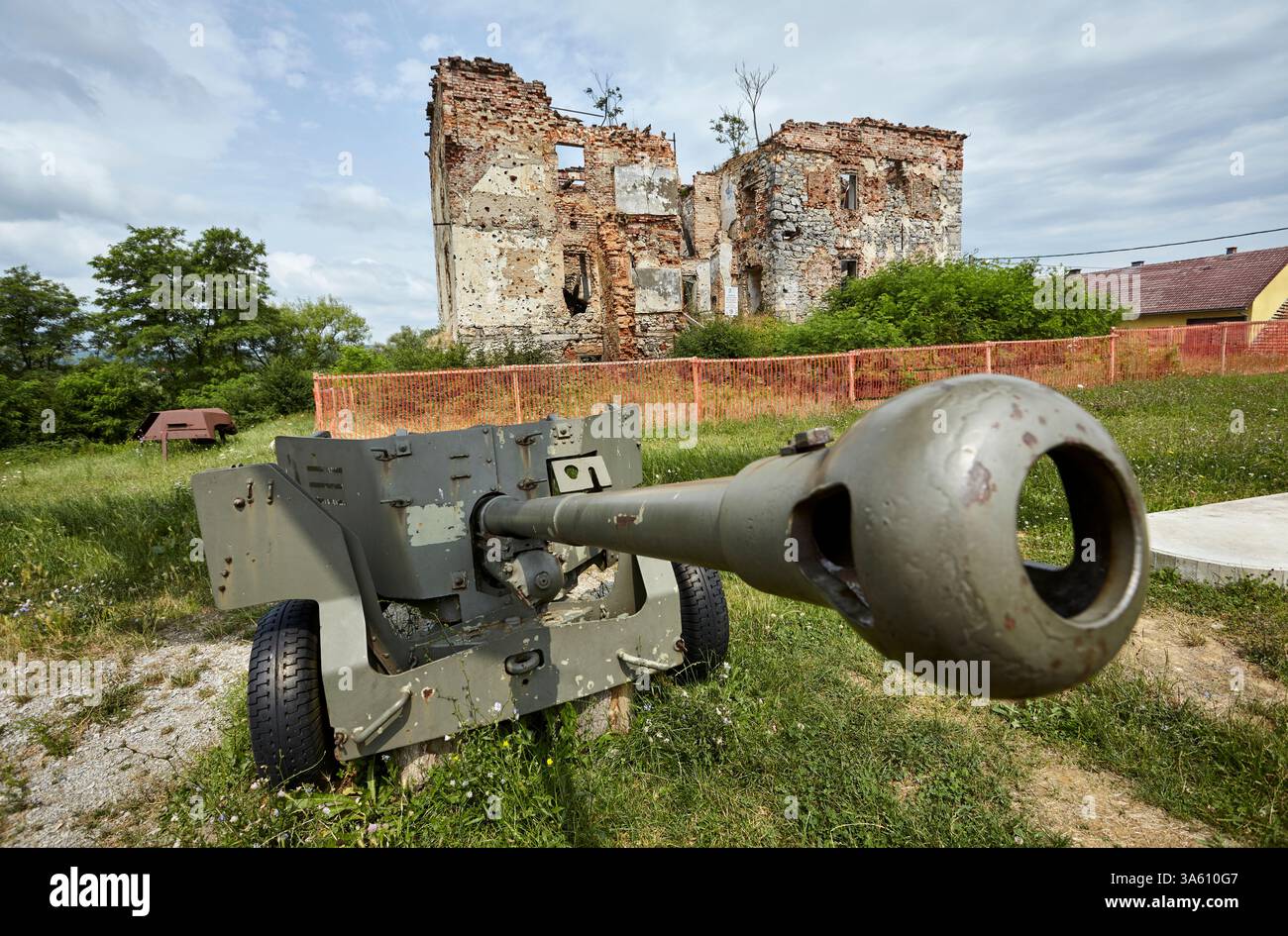 An artillery gun positioned in a field near war-ravaged ruins under a ...
