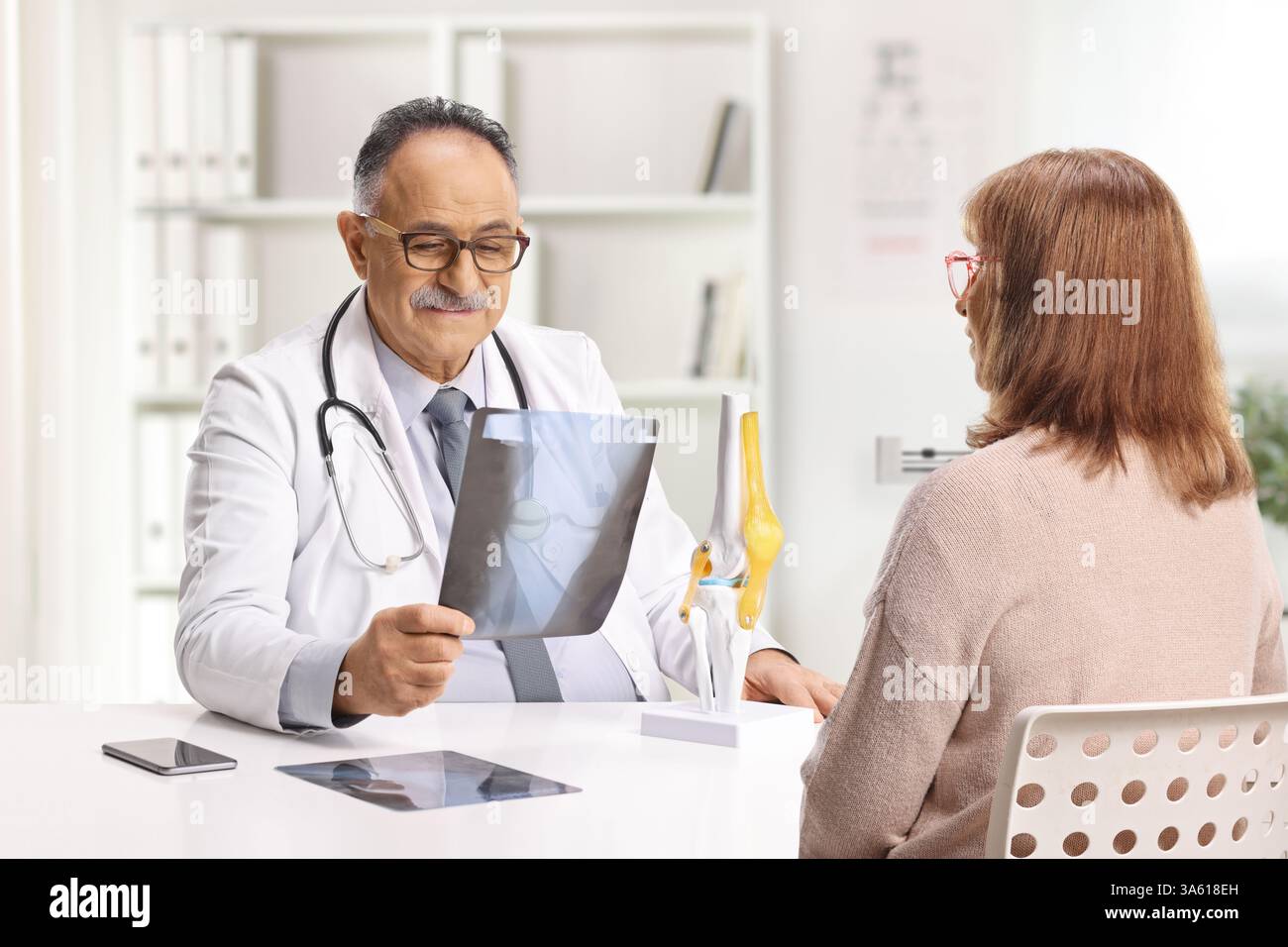 Doctor sitting behind a desk and checking an x-ray image from a knee ...
