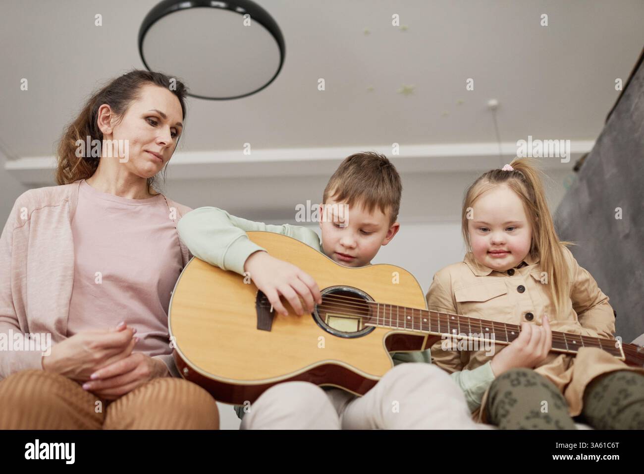 Low angle portrait of boy playing guitar at home with mother and sister ...