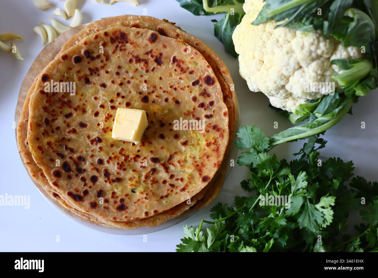 Gobi paratha served alongside a fresh cauliflower bulb with leaves. A ...
