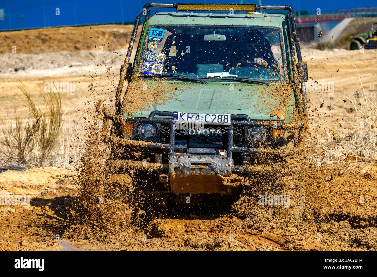 Green off-road vehicle stuck in a huge hole with mud and water, crossing difficult terrain by ...