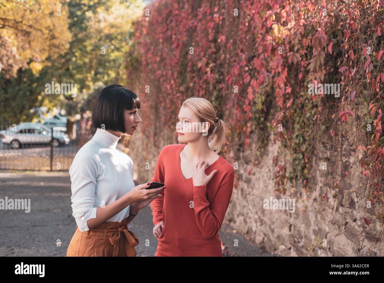 Two excited girls using mobile phones in park. Girls friends using ...