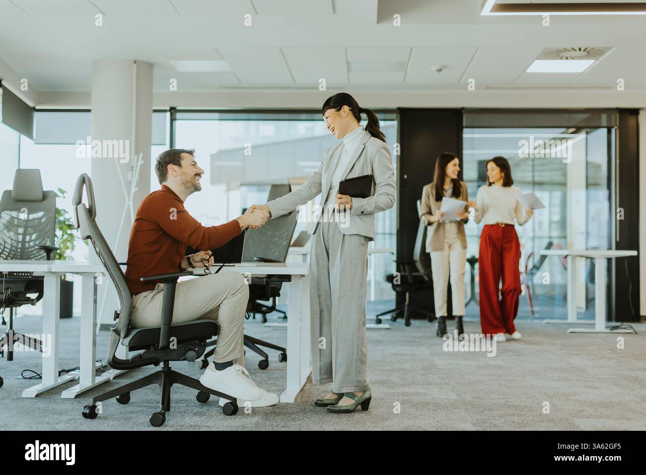 Bright office environment sees a joyful handshake between a male and ...
