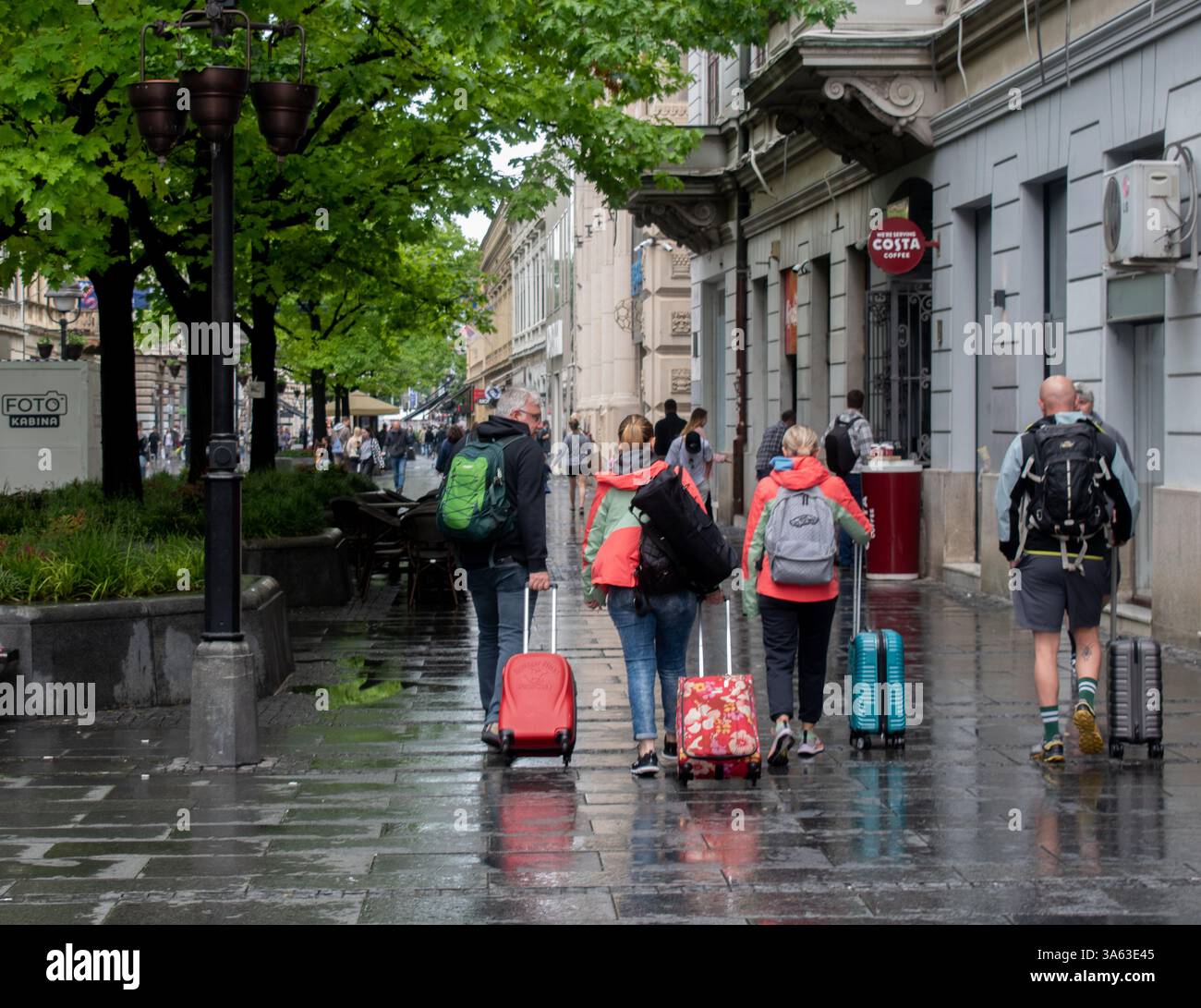 a group of people walking down the street of Belgrade with suitcases in ...