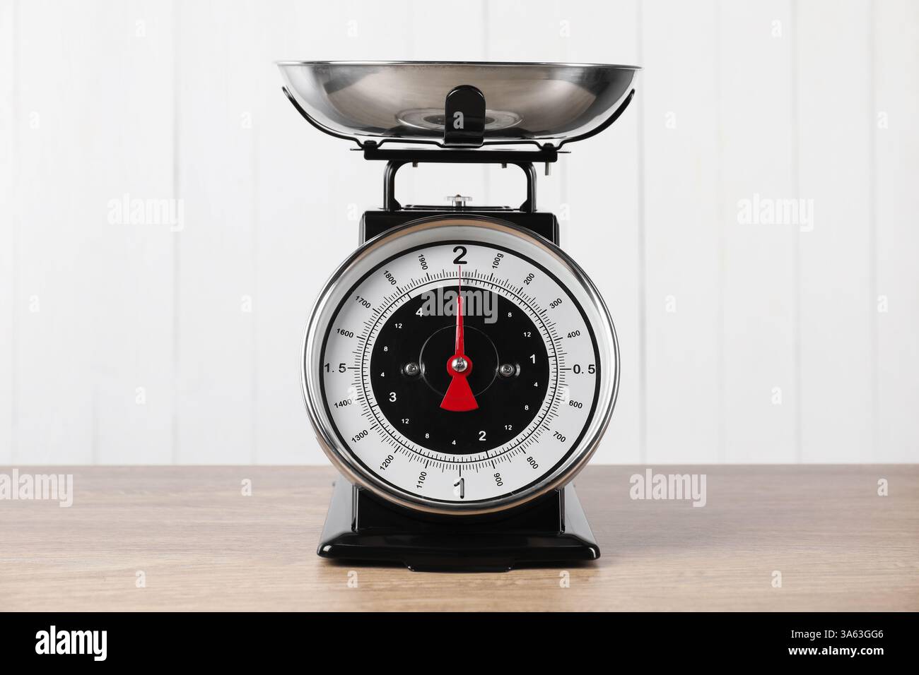 Mechanical kitchen scale with bowl on wooden table against white ...