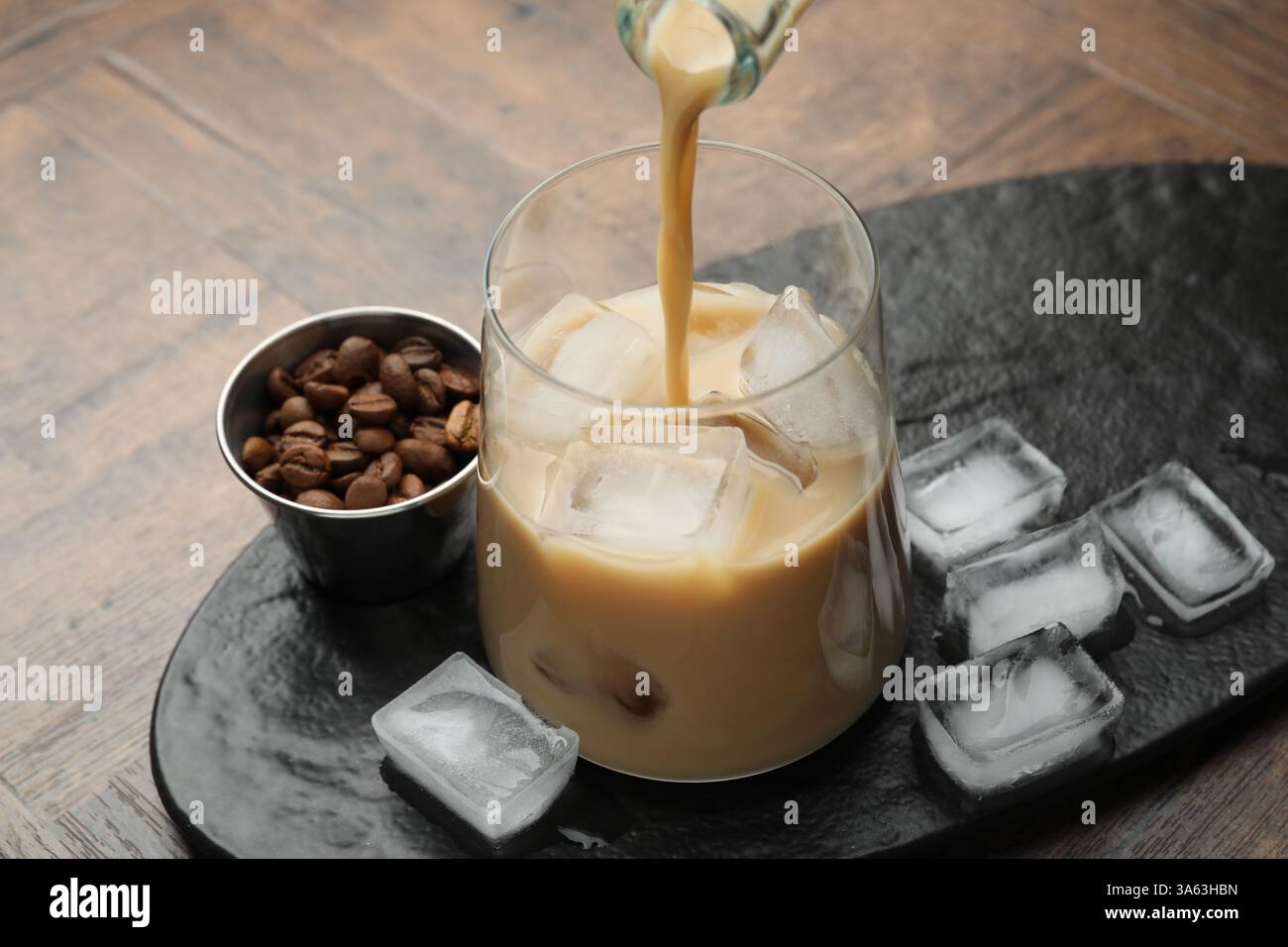 Pouring coffee cream liqueur from bottle into glass at wooden table ...