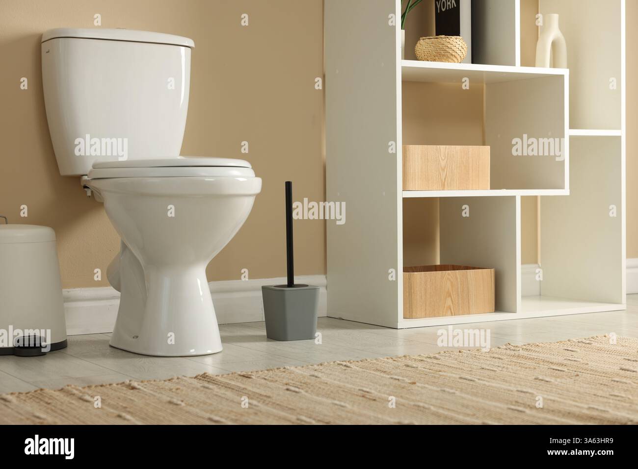 Toilet bowl, brush and trash bin near beige wall in restroom Stock ...