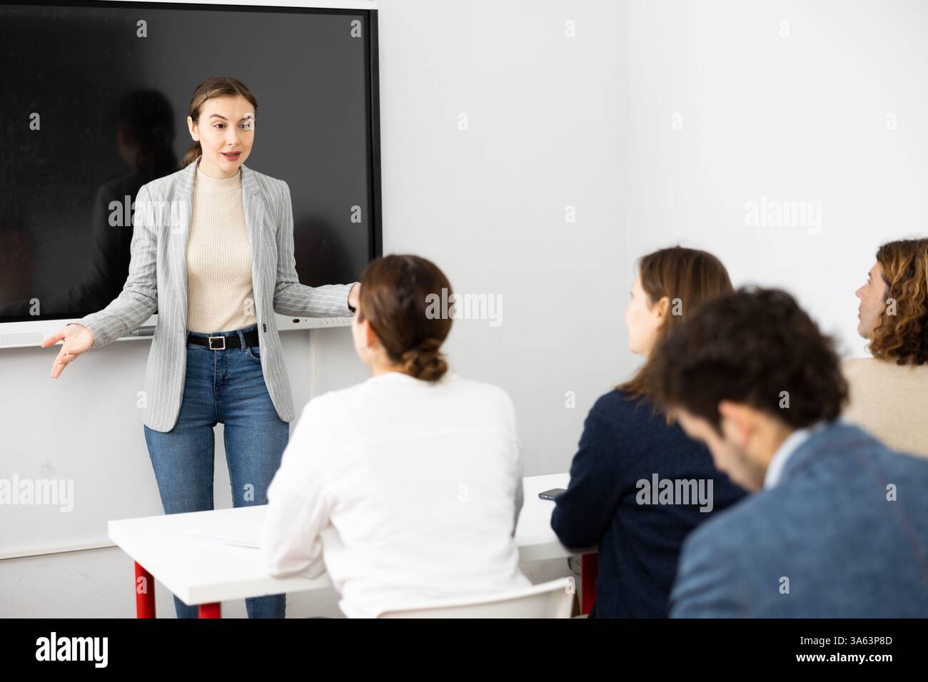 Young female professor explaining subject to classroom full of students ...