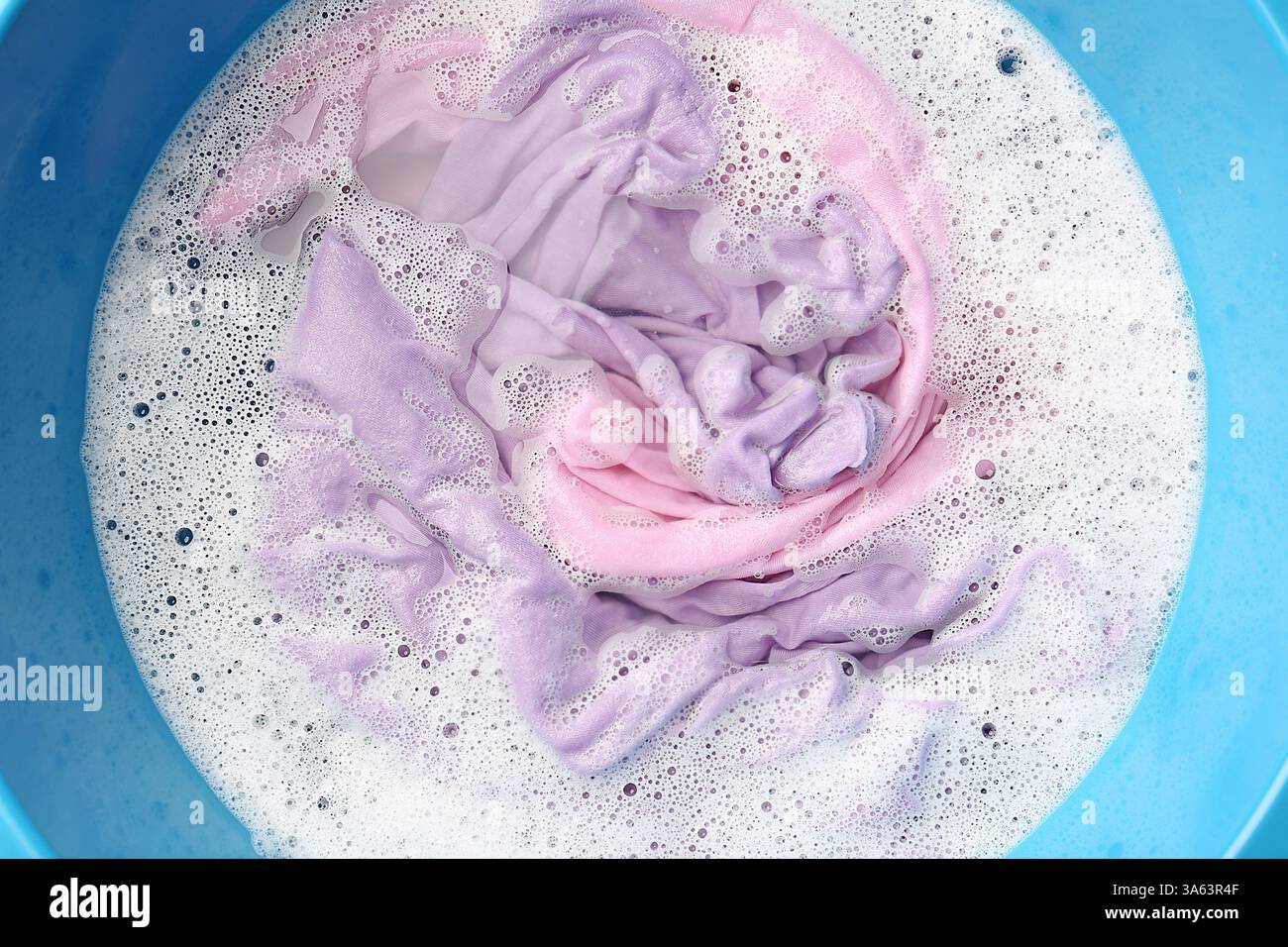 Colorful clothes soaked in water before washing, top view Stock Photo ...
