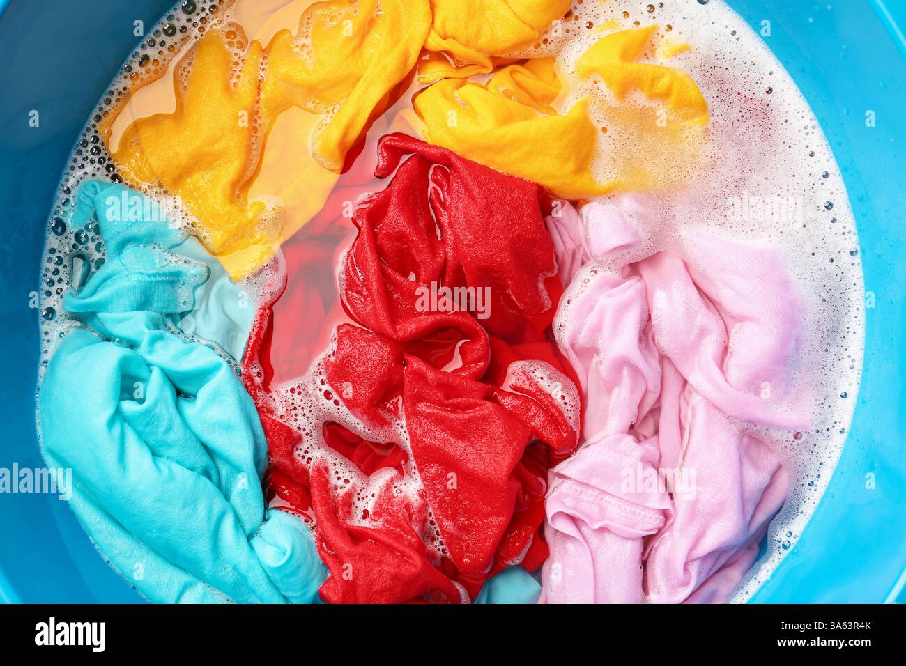 Colorful clothes soaked in water before washing, top view Stock Photo ...