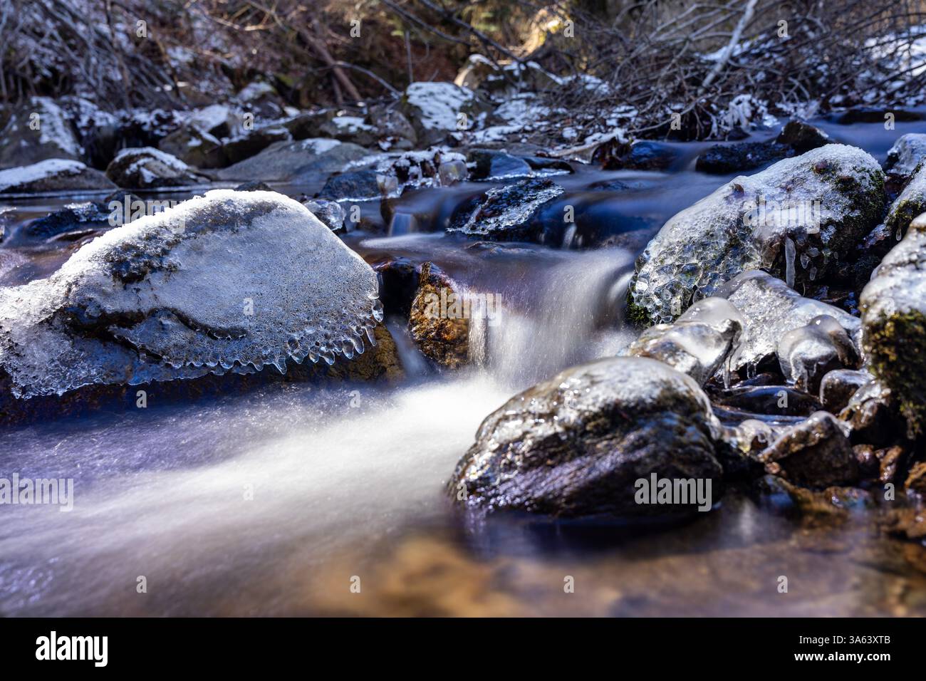 Melting snow and ice create icicles on rocks in a flowing stream ...