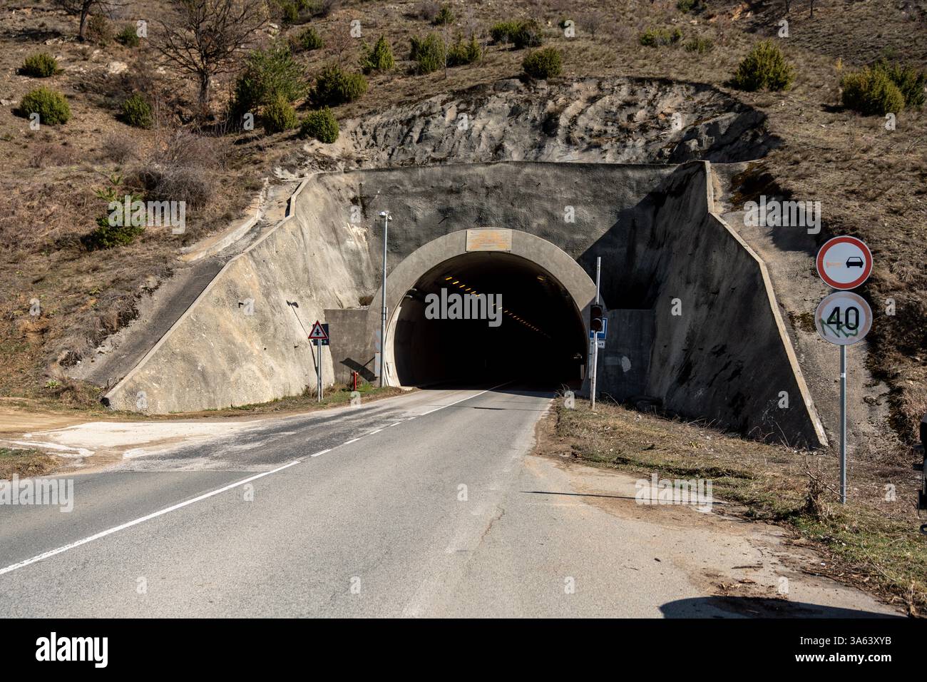 Empty asphalt road winding toward a tunnel entrance nestled in the ...