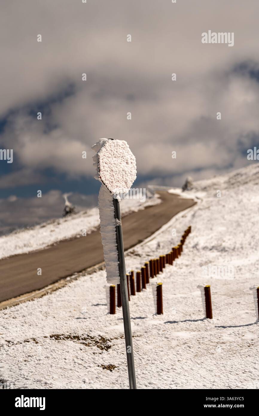Snow and ice covering a road sign and delineators along a mountain road ...