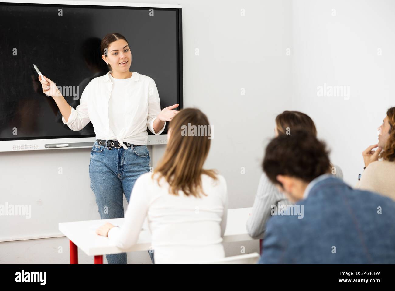 Young female professor explaining subject to classroom full of students ...
