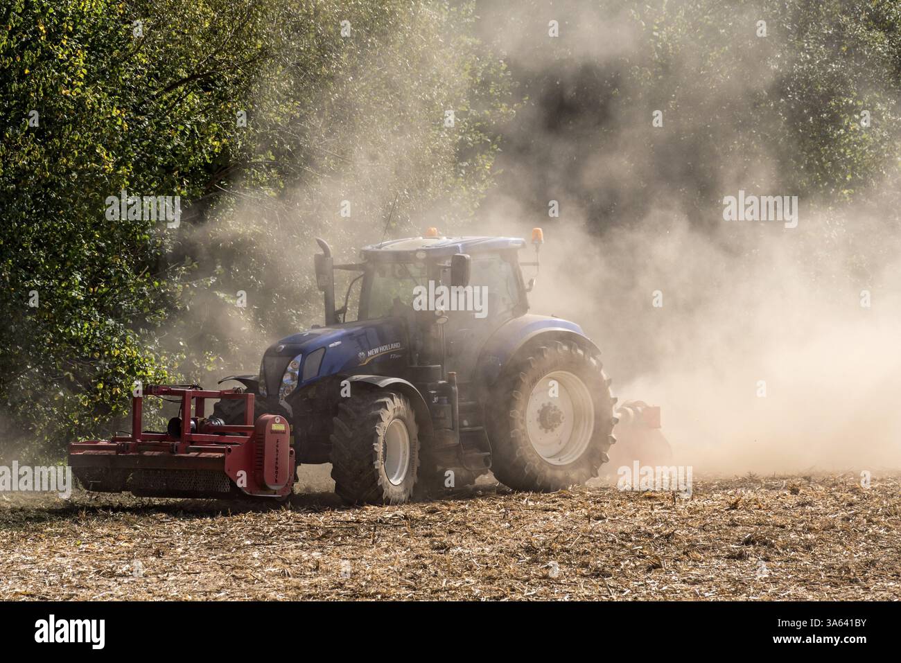 Tractor with plough digging up dried-out soil, large cloud of dust ...