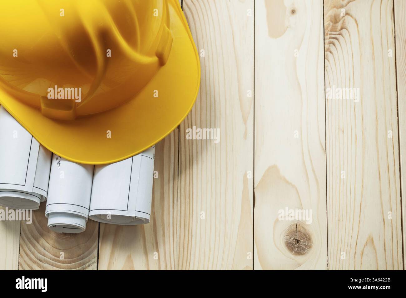 Yellow construction helmet and white rolled blueprints on wooden boards ...