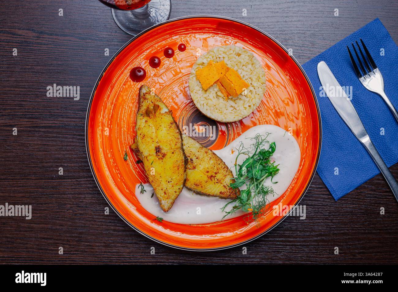 Grilled fresh red fish lies on a plate along with a side dish and sauce ...