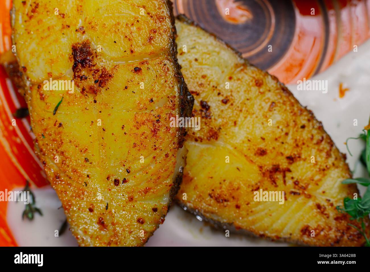 Grilled fresh red fish lies on a plate along with a side dish and sauce ...