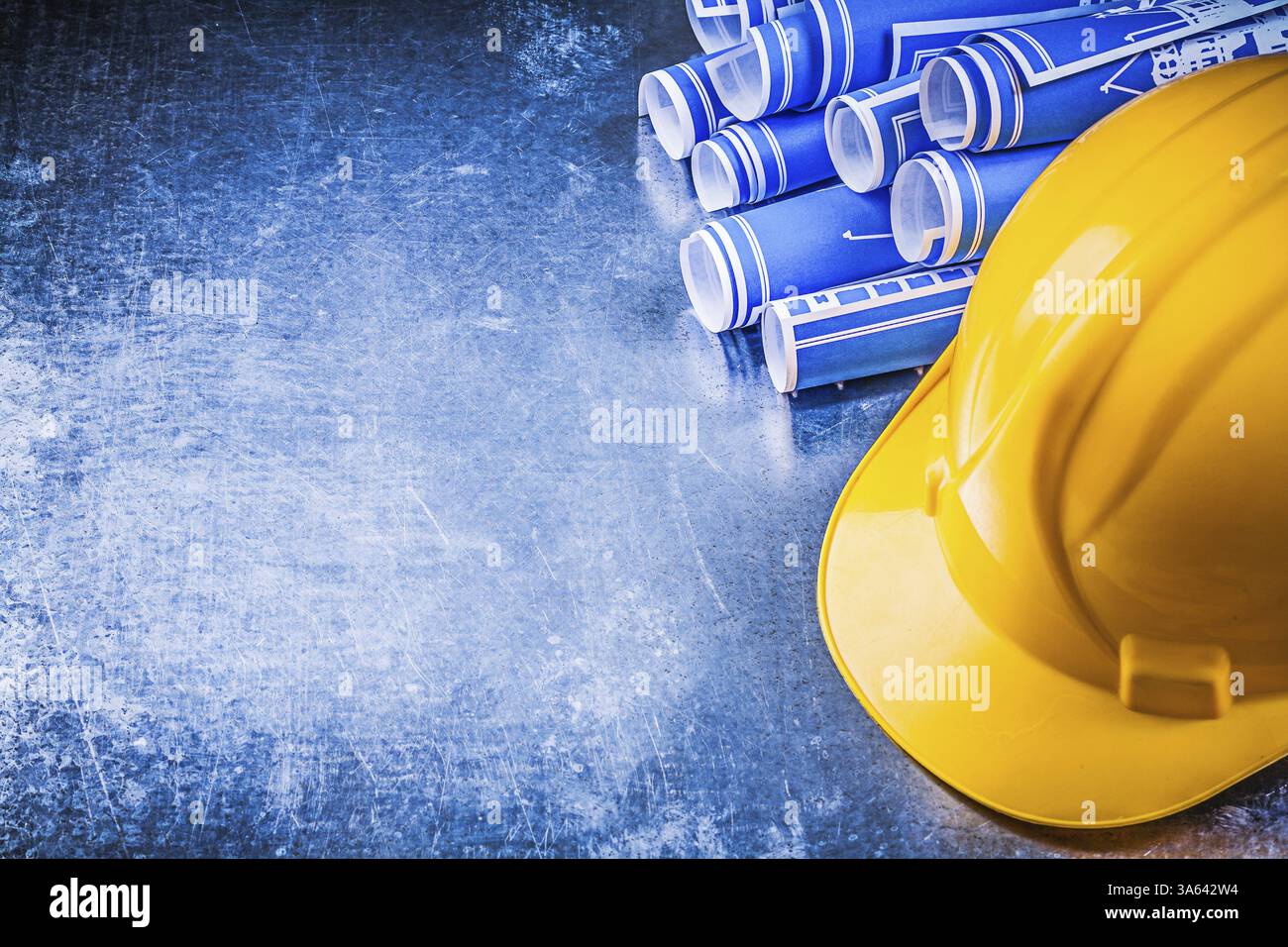 Blue engineering drawings yellow hard hat on scratched metallic background construction concept ...