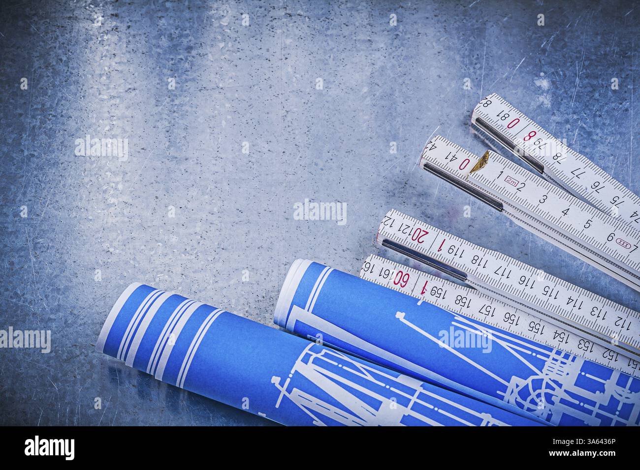 Blue rolled construction drawings wooden meter on scratched metallic ...