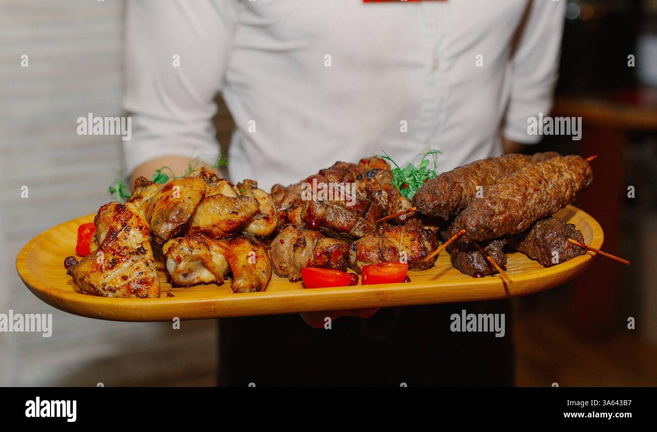 Shish kebab from different types of meat lies on a tray held by a young ...
