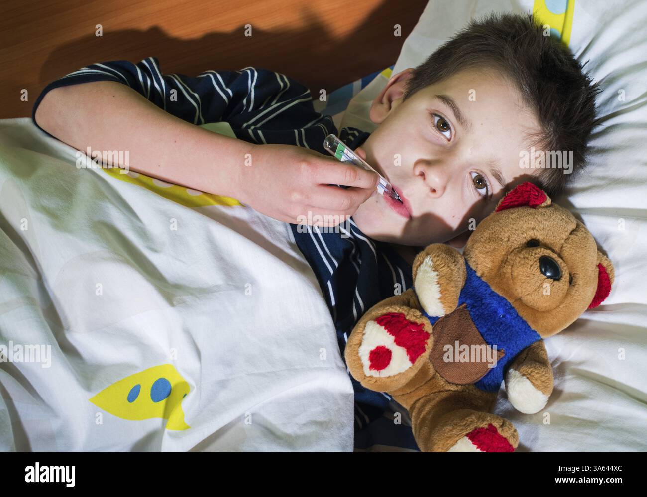 Sick child in bed with teddy bear. Measuring the temperature with a ...