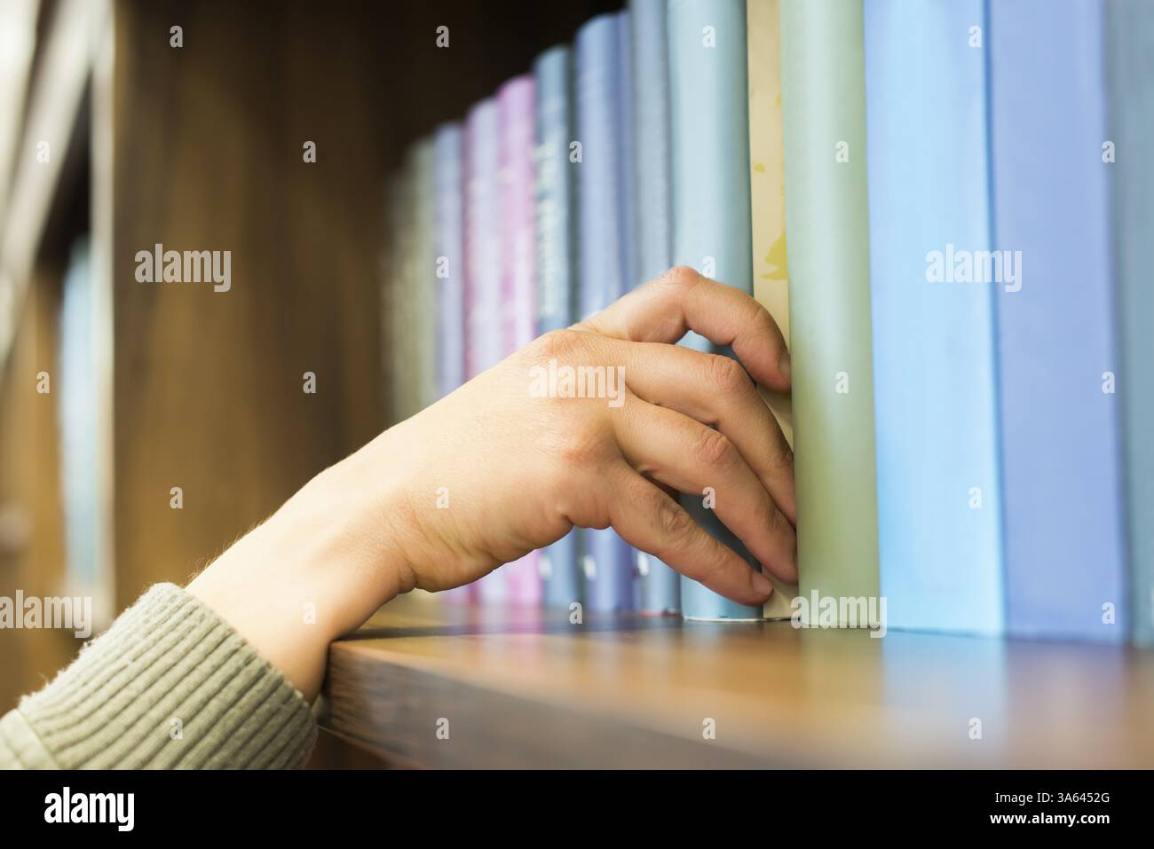 Hand pulling a book off the shelf. Blue colors books Stock Photo - Alamy