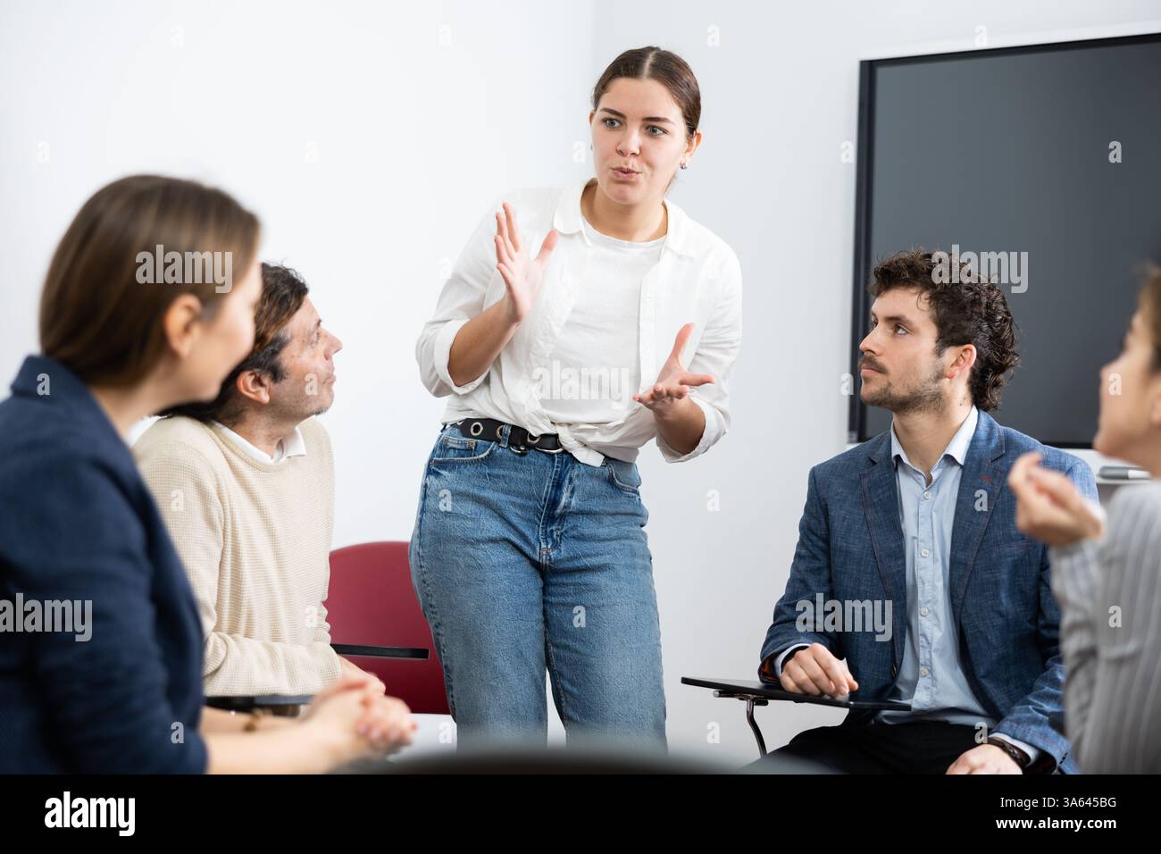 Young female professor explaining subject to classroom full of students ...