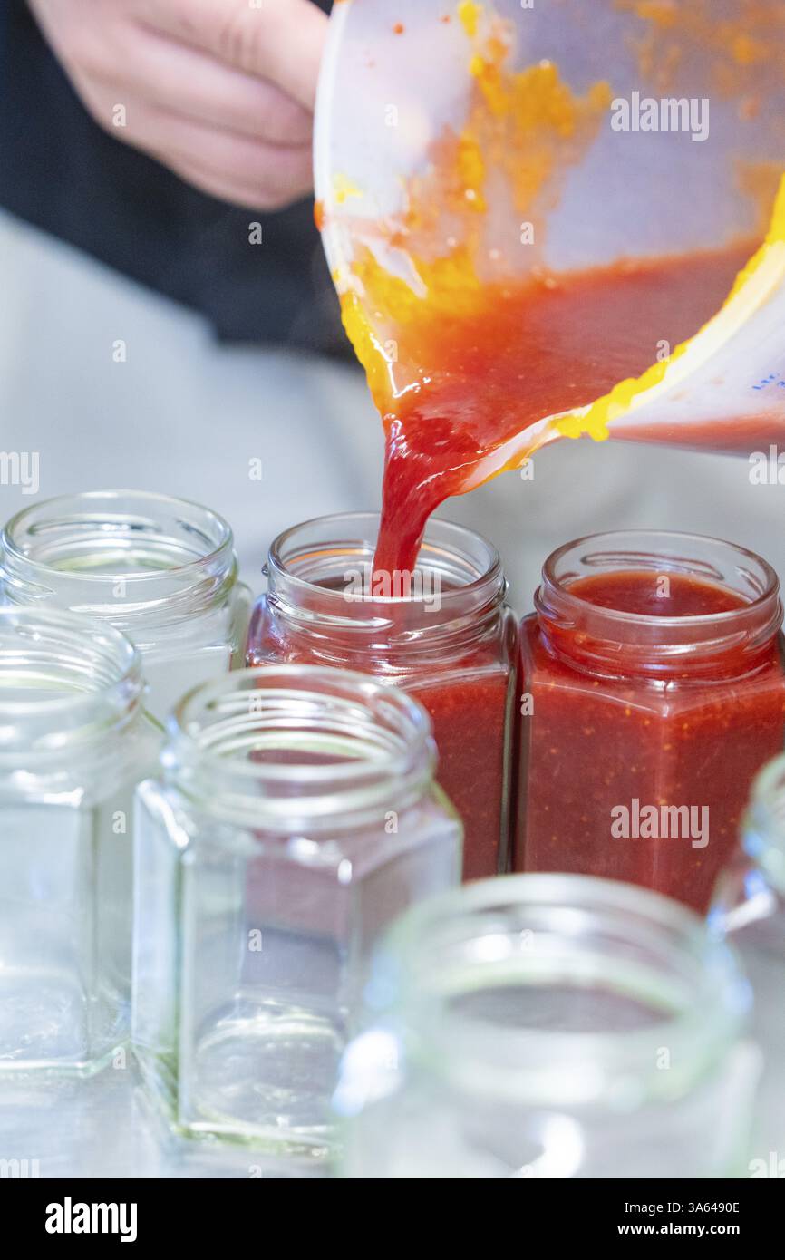 Red liquid is poured from a measuring cup into empty jars, jam ...