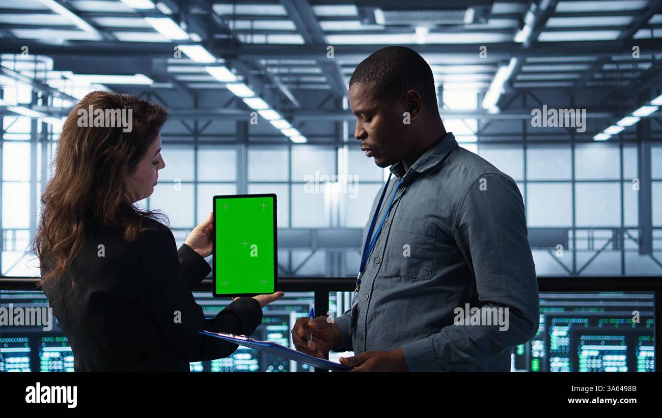 Engineers using green screen tablet in data center, checking infrastructure reliability, writing ...