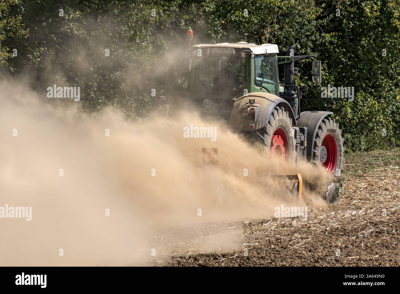 Tractor with plough digging up dried-out soil, large cloud of dust ...