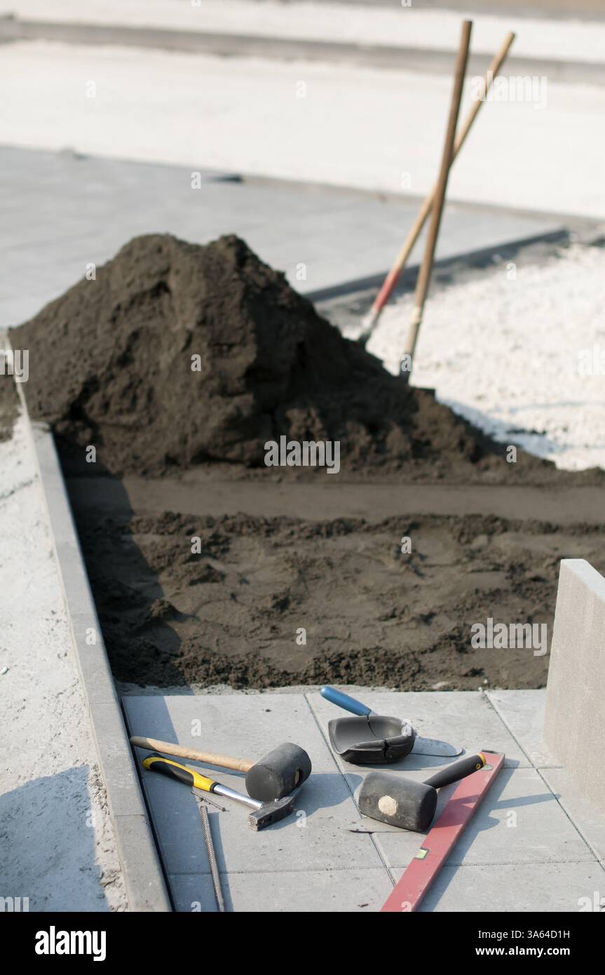 Tiling of pavement and sand pile. Two shovels and Construction tools ...