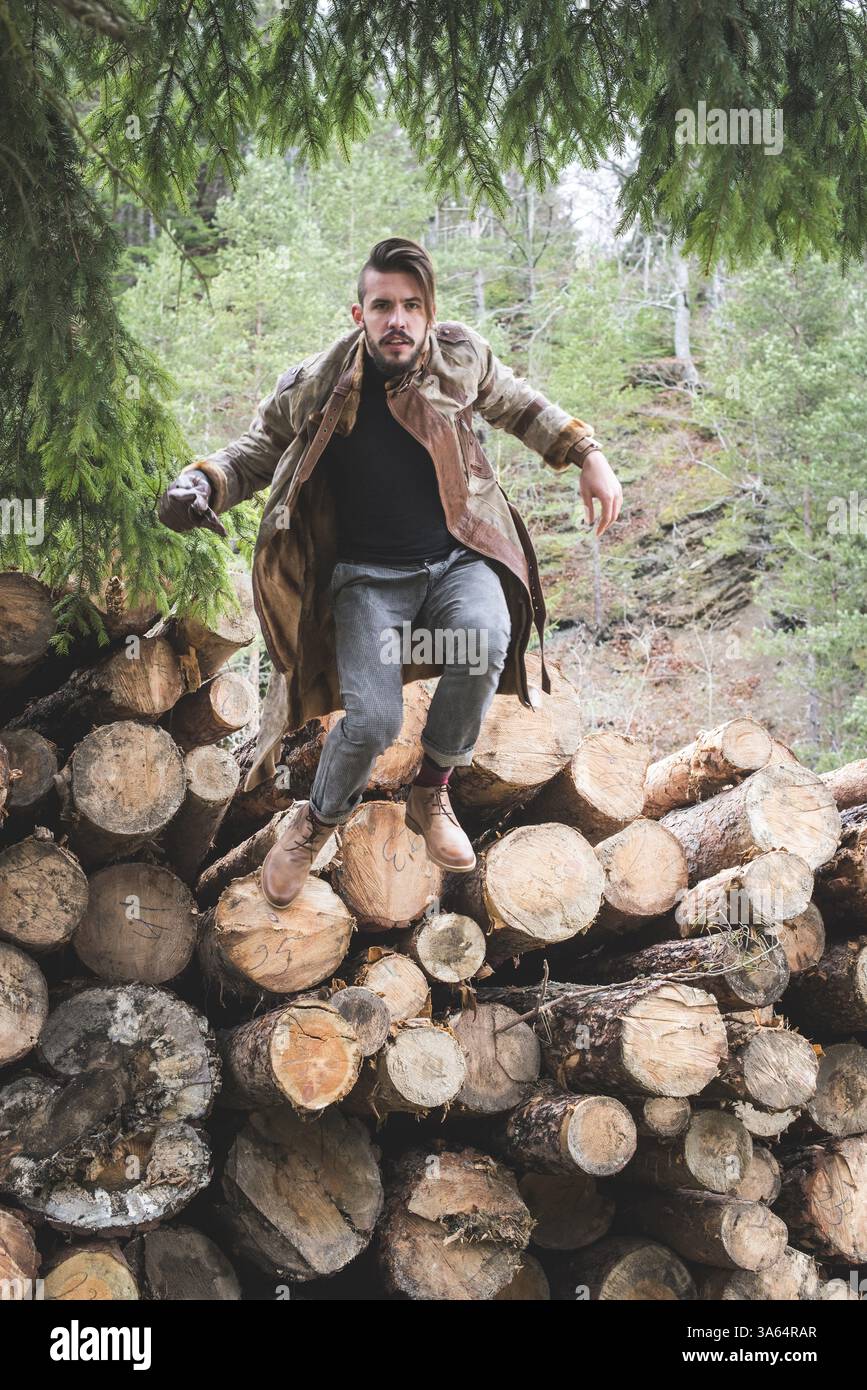 Young men on logs in the forest. Leather and jeans. Pine tree on top ...