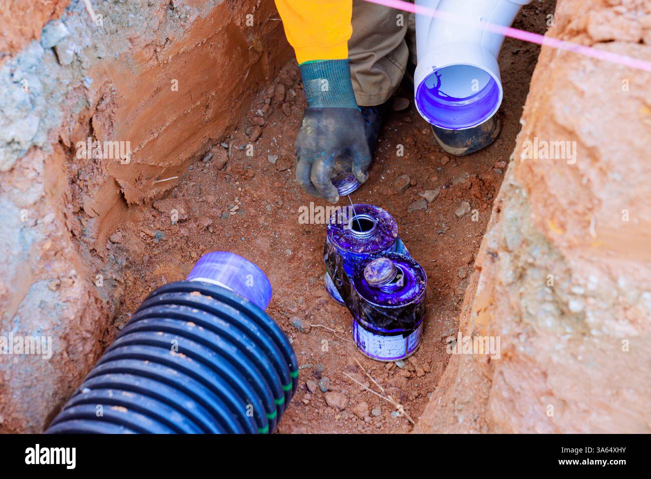 Worker installs pipes, fittings in trench at construction site during ...
