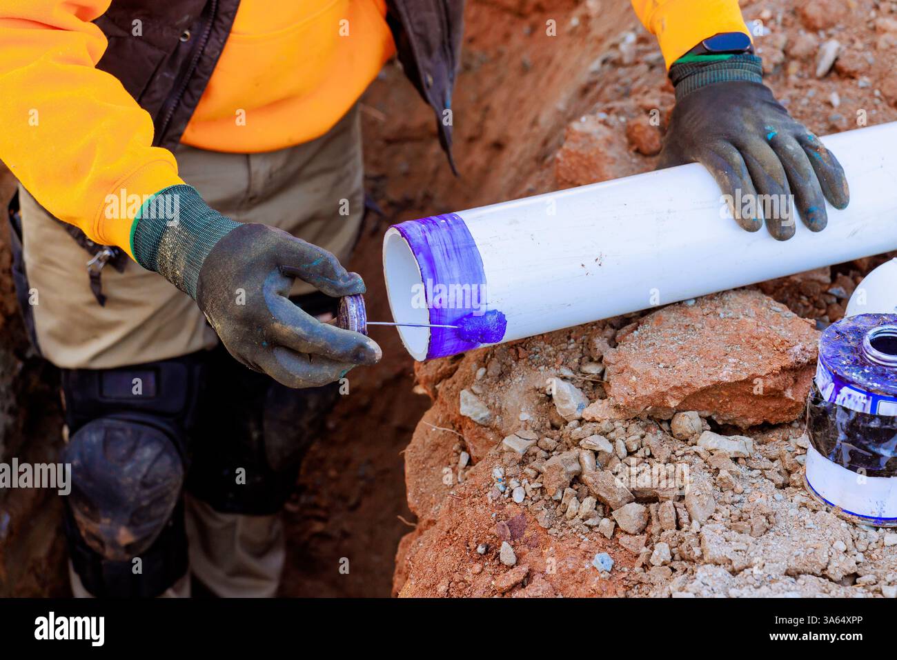 Construction worker prepares PVC piping by applying purple primer to ...