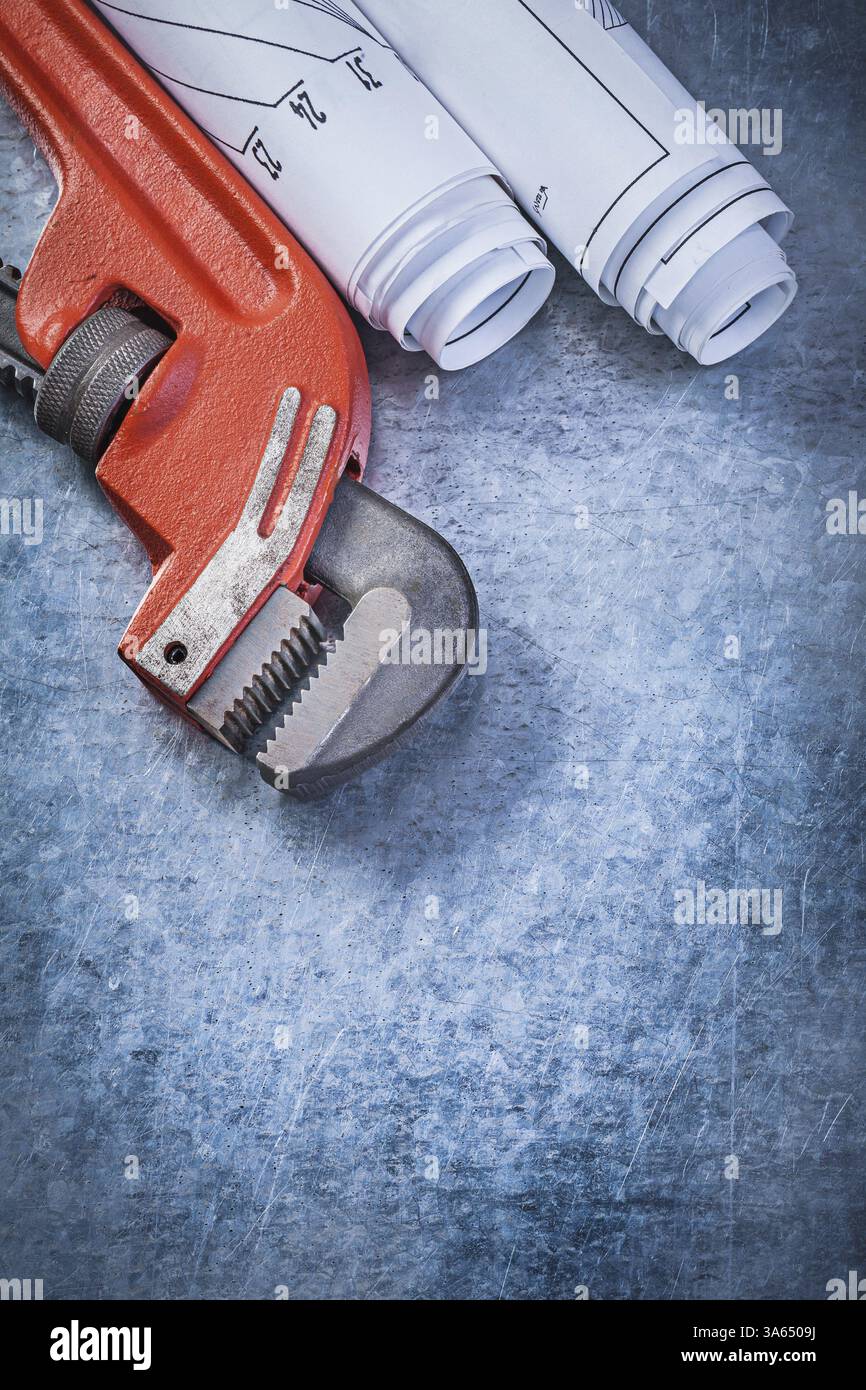 Pipe wrench rolled up engineering drawings on metallic background ...