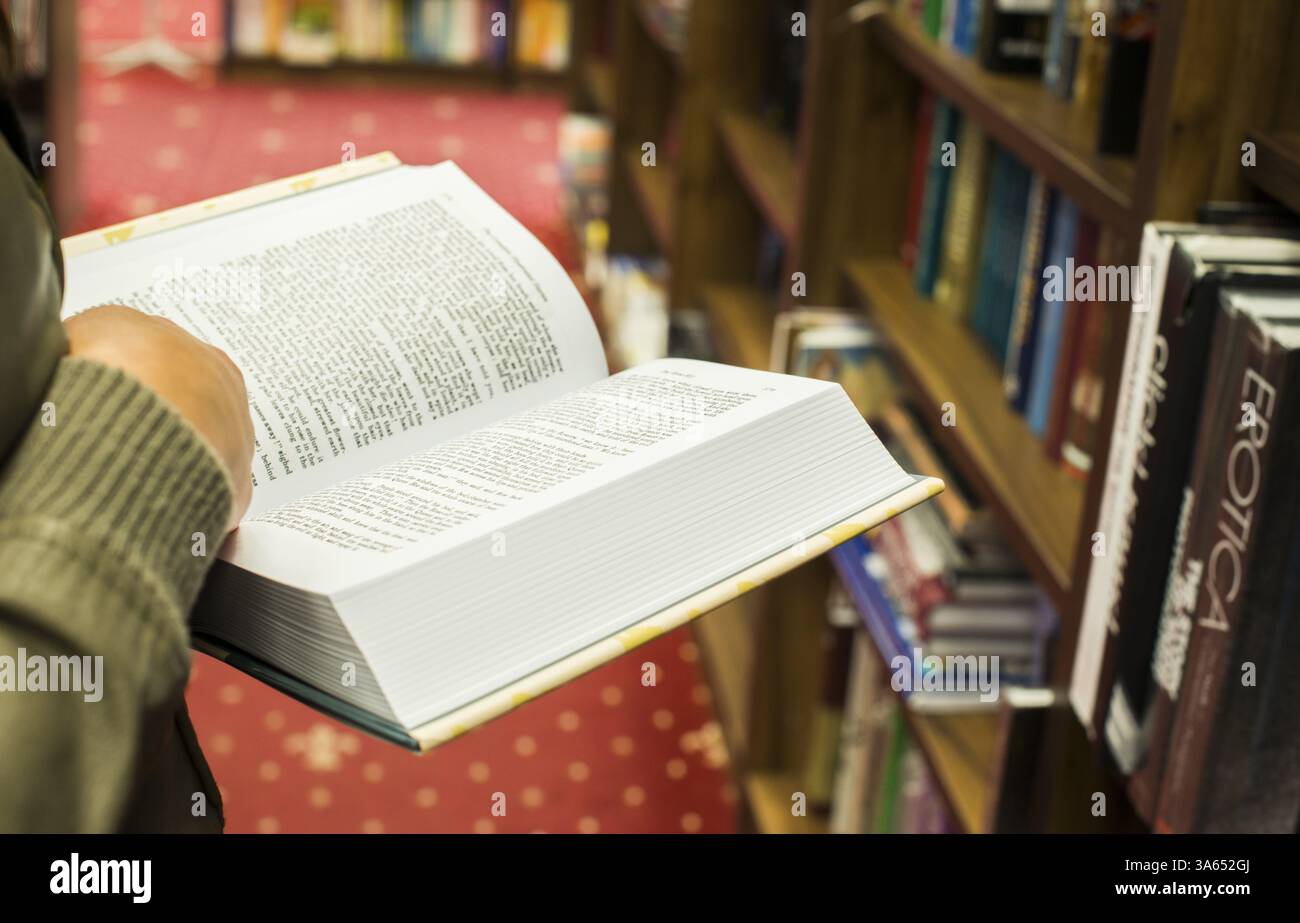 Hand holding open book in a bookstore. Many books on the background ...