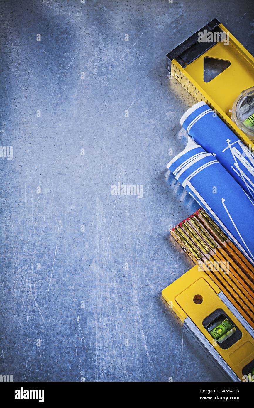 Blue rolled blueprints levels yellow wooden meter on metallic surface ...